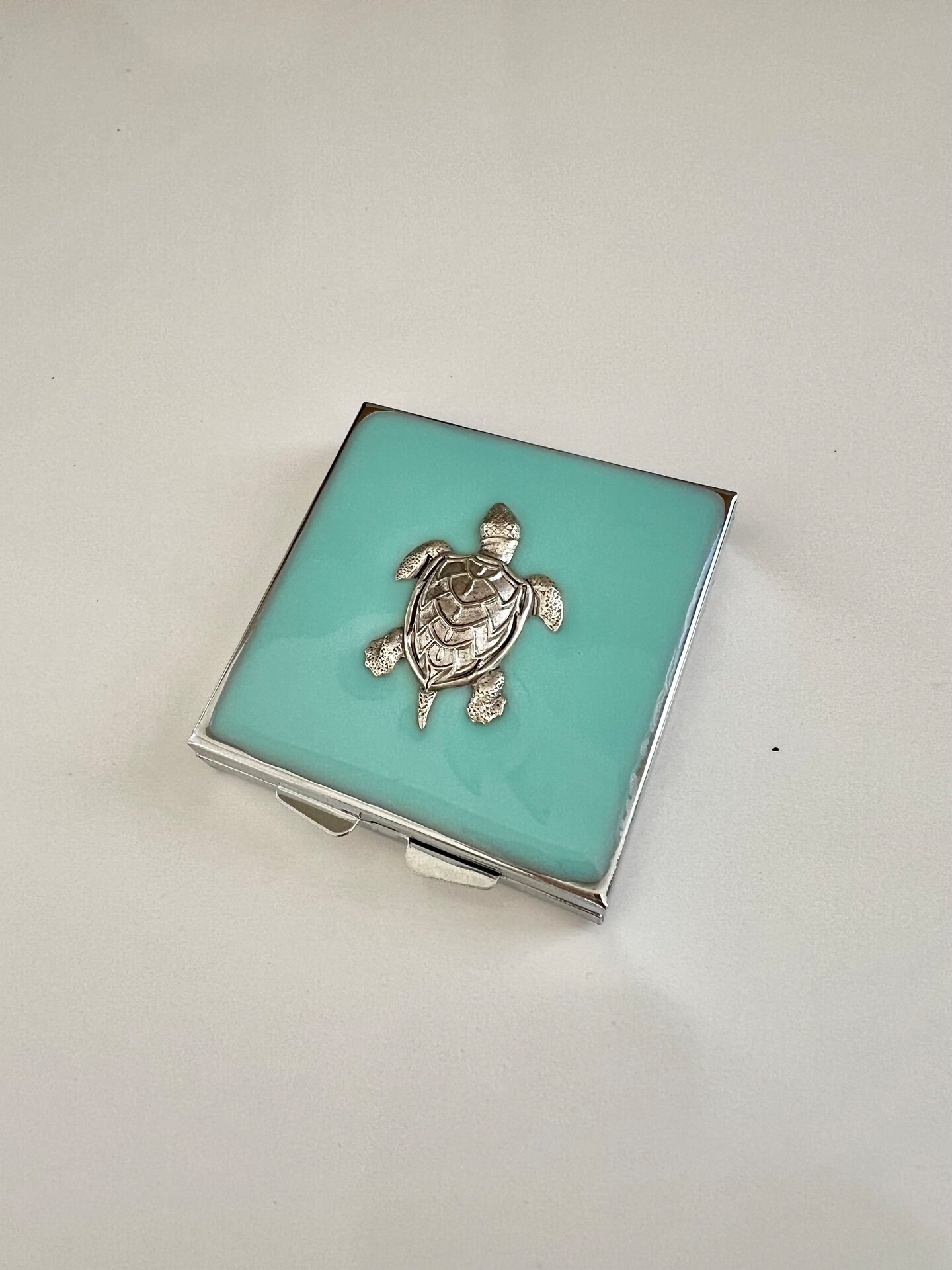 Pill box with silver sea turtle set on a blue resin background ...