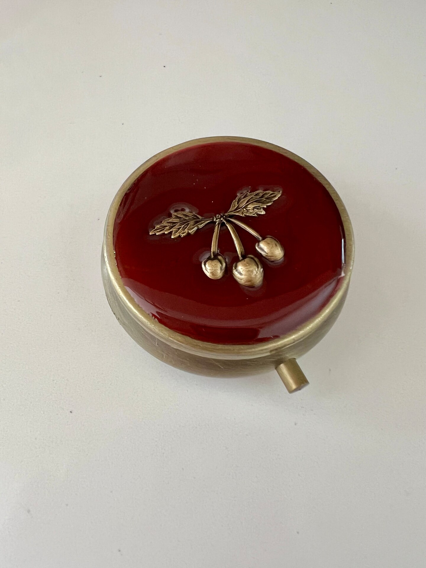 Pill box embellished with brass cherries set on a cherry red resin ...