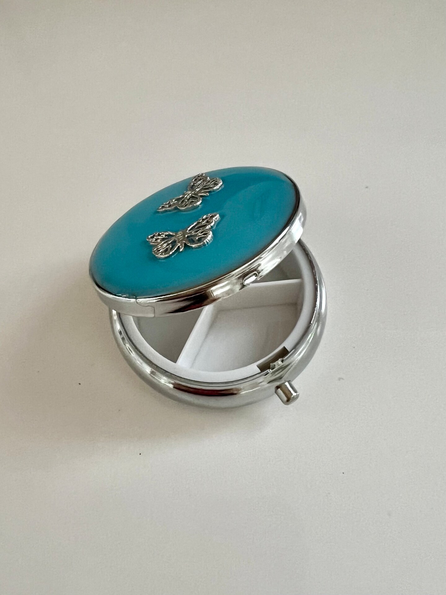 Pill box with two silver butterflies set on a blue resin background ...