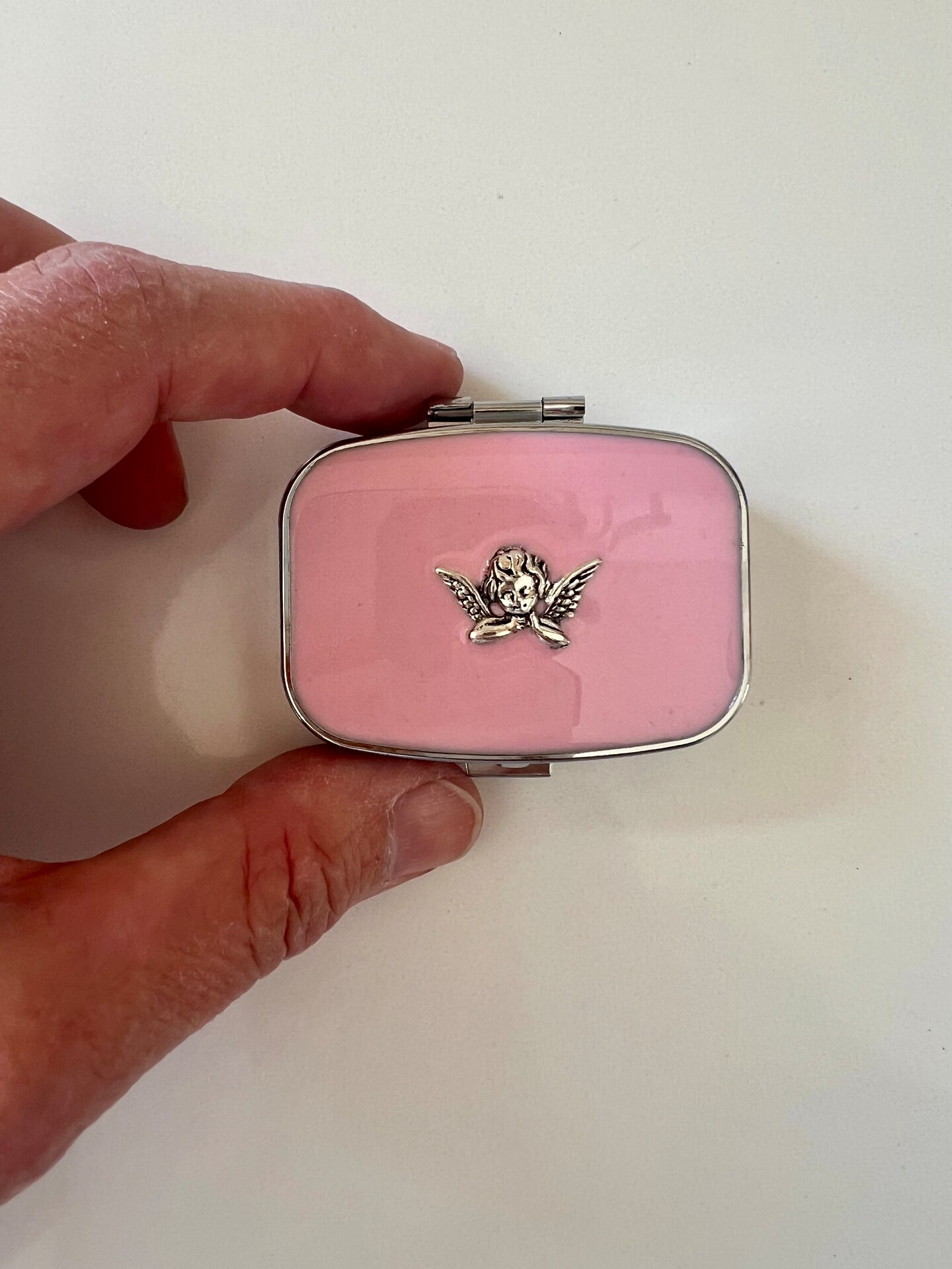 Metal pill box with a silver cherub angel on a pink resin background ...